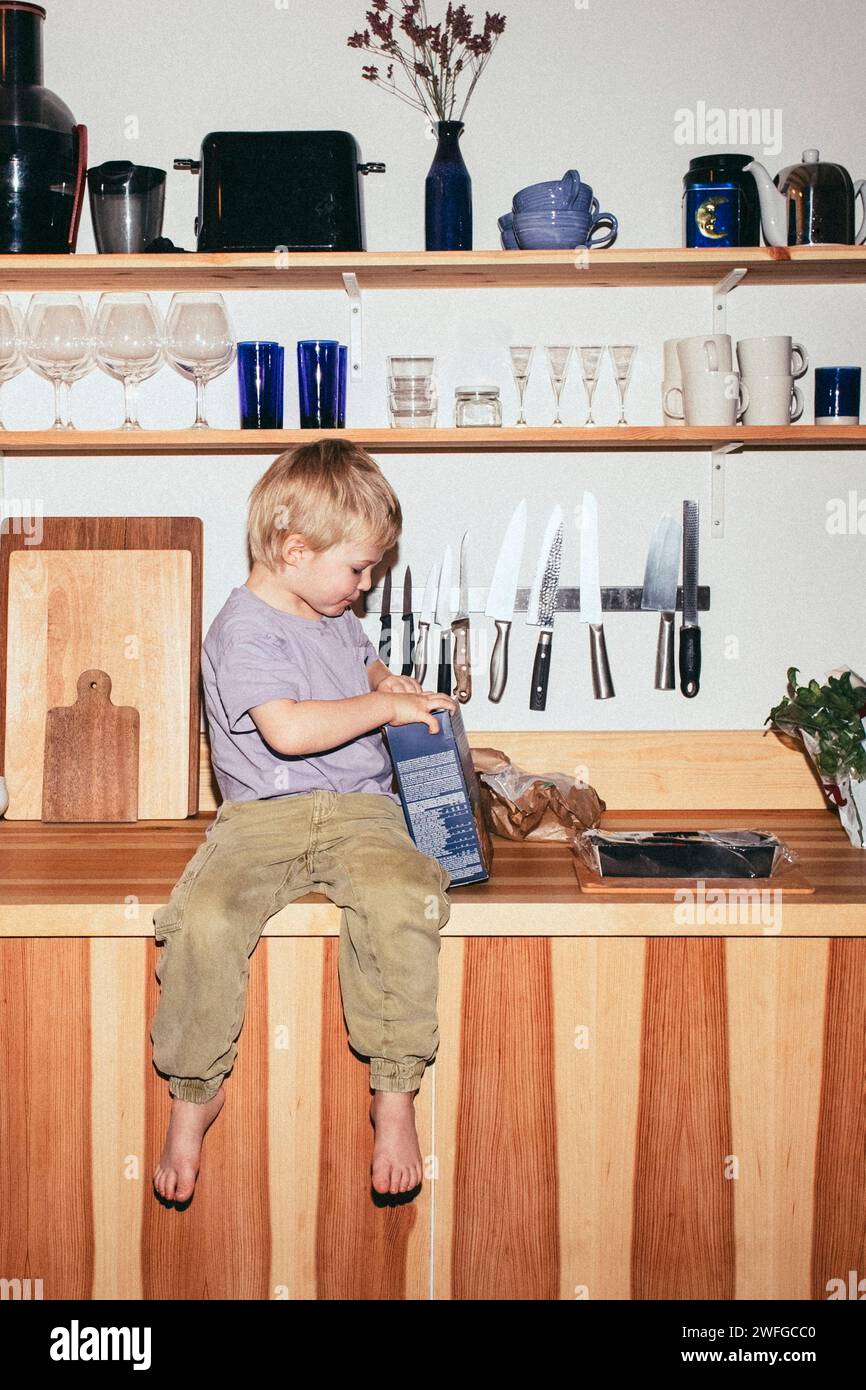 Boy opening food packet while sitting on kitchen counter at home Stock ...