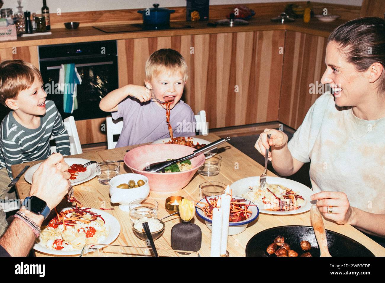 Playful kids having meal with parents while sitting at dining table in ...
