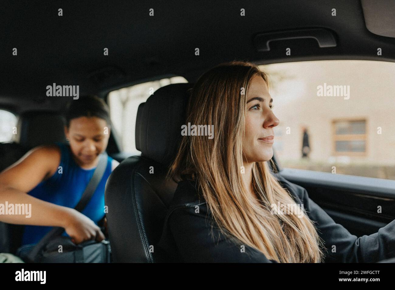 Female blond coach driving while teenage girl sitting behind in car ...