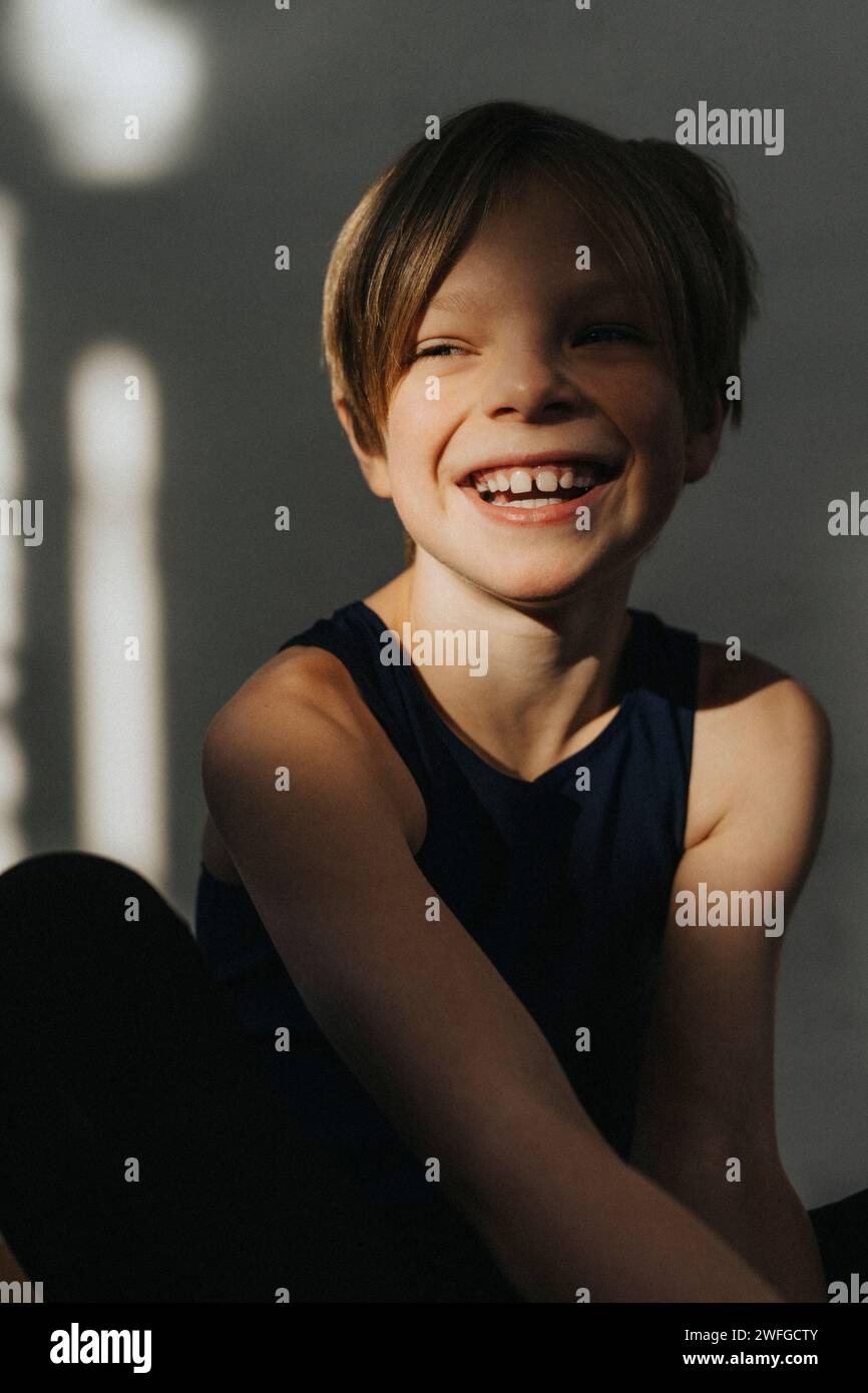 Happy elementary boy looking away while sitting against wall Stock ...