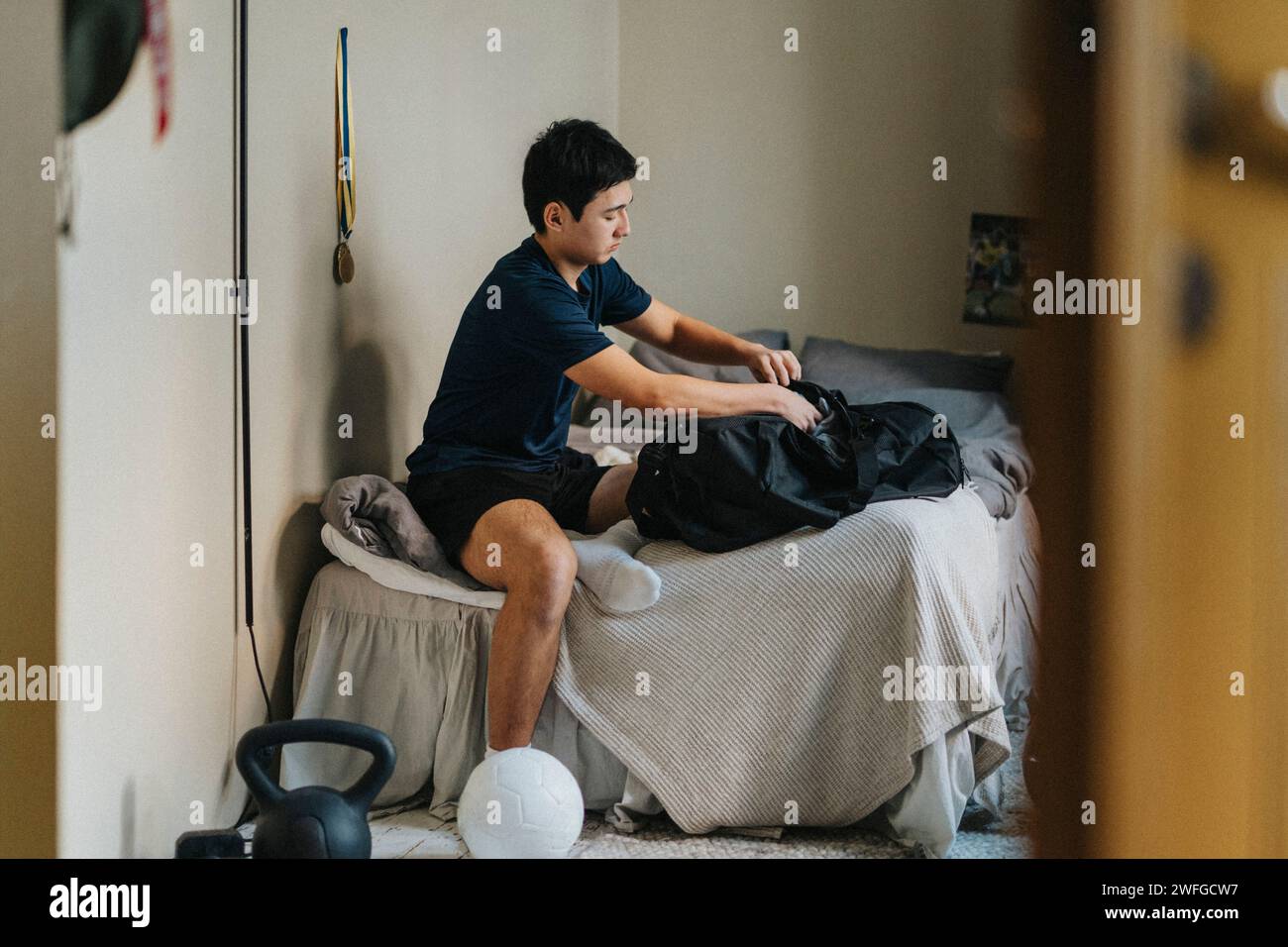 Teenage boy with backpack sitting on bed in bedroom at home Stock Photo ...