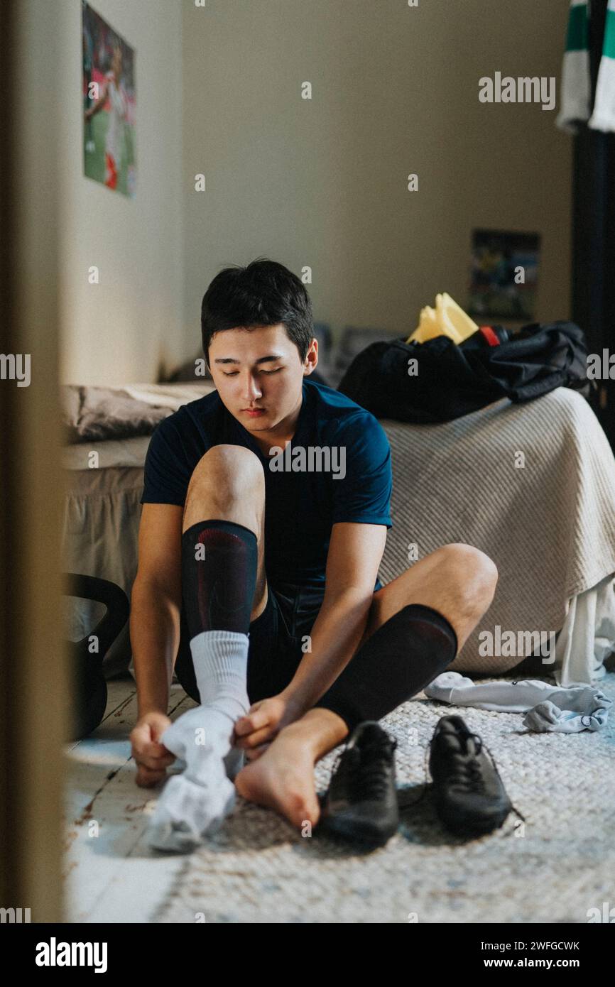 Teenage boy wearing sock while sitting on carpet at home Stock Photo ...