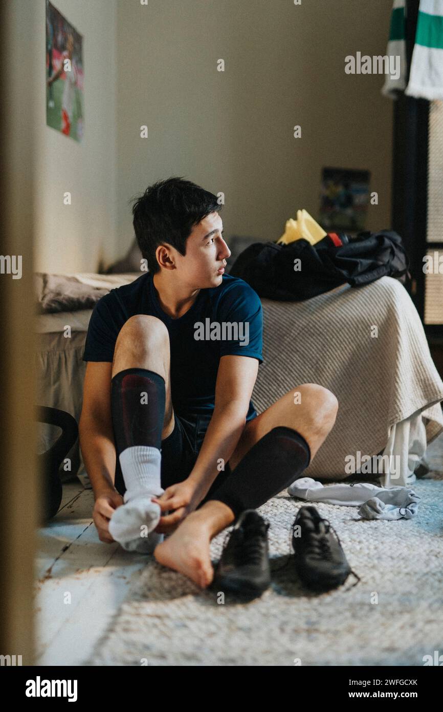 Teenage boy wearing sock while sitting on ground at home Stock Photo ...