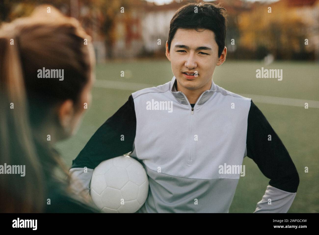 Male athlete talking with female coach while standing in sports field ...
