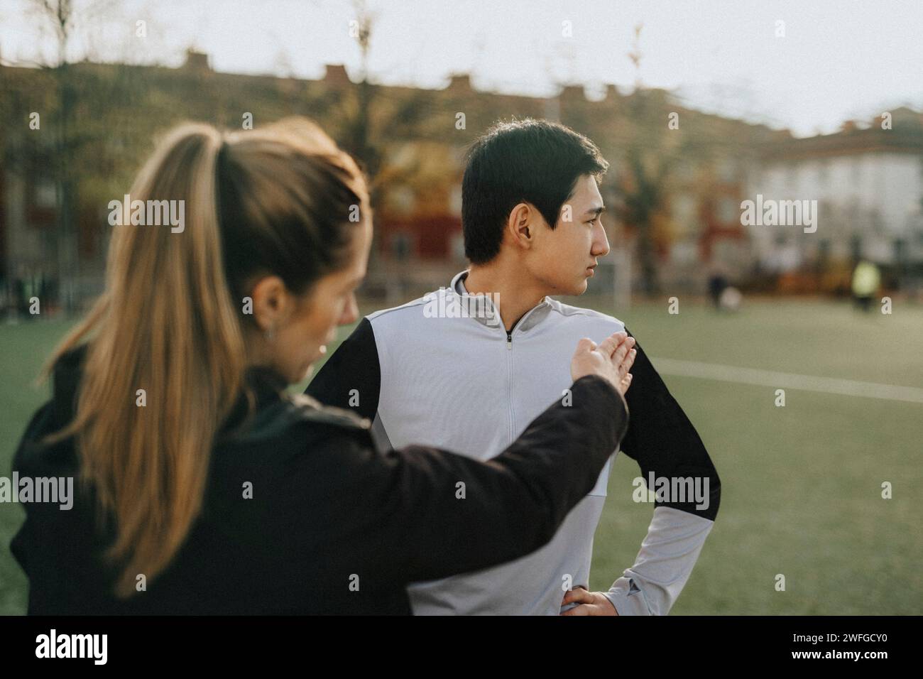 Female coach talking with male athlete while standing in sports field ...