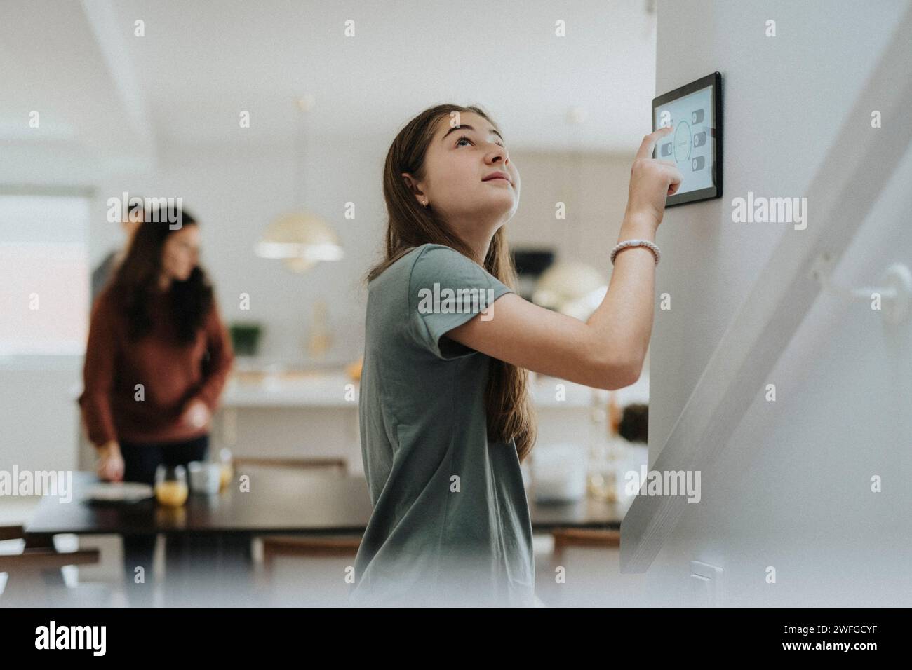 Girl adjusting room temperature through digital tablet mounted on wall ...