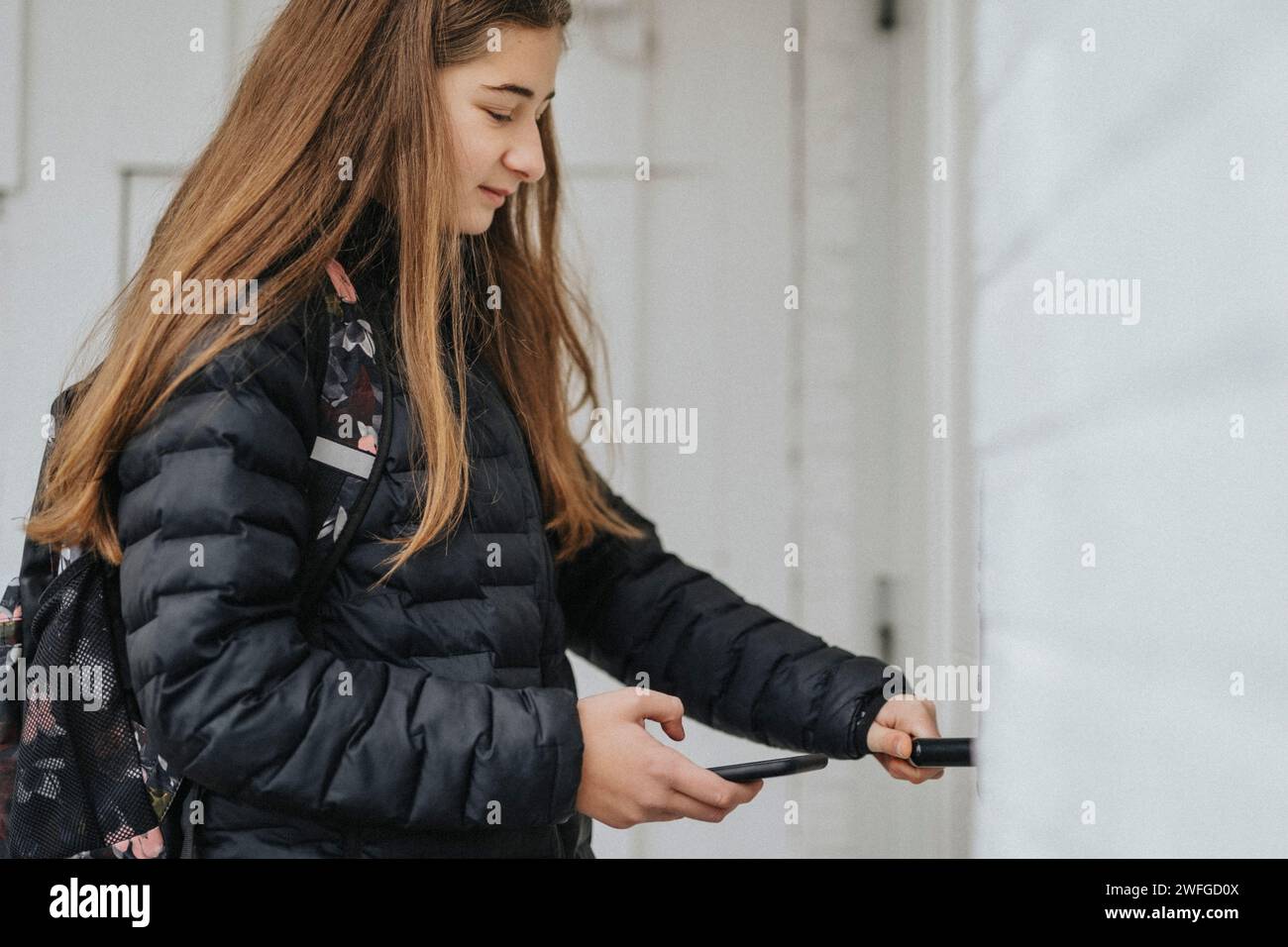 Girl unlocking door lock through smart phone while standing at home ...