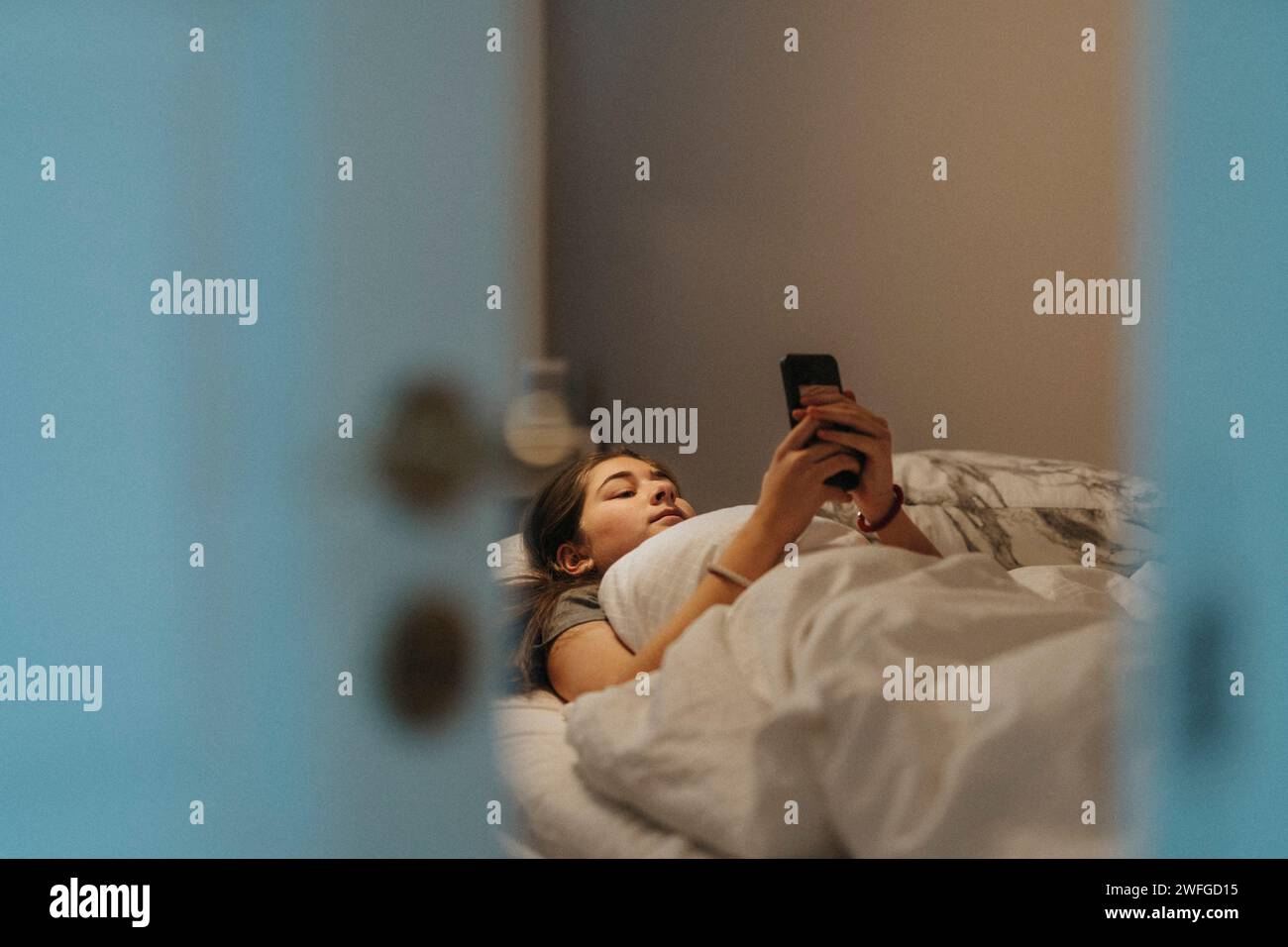 Girl using smart phone while lying on bed in bedroom at modern home ...