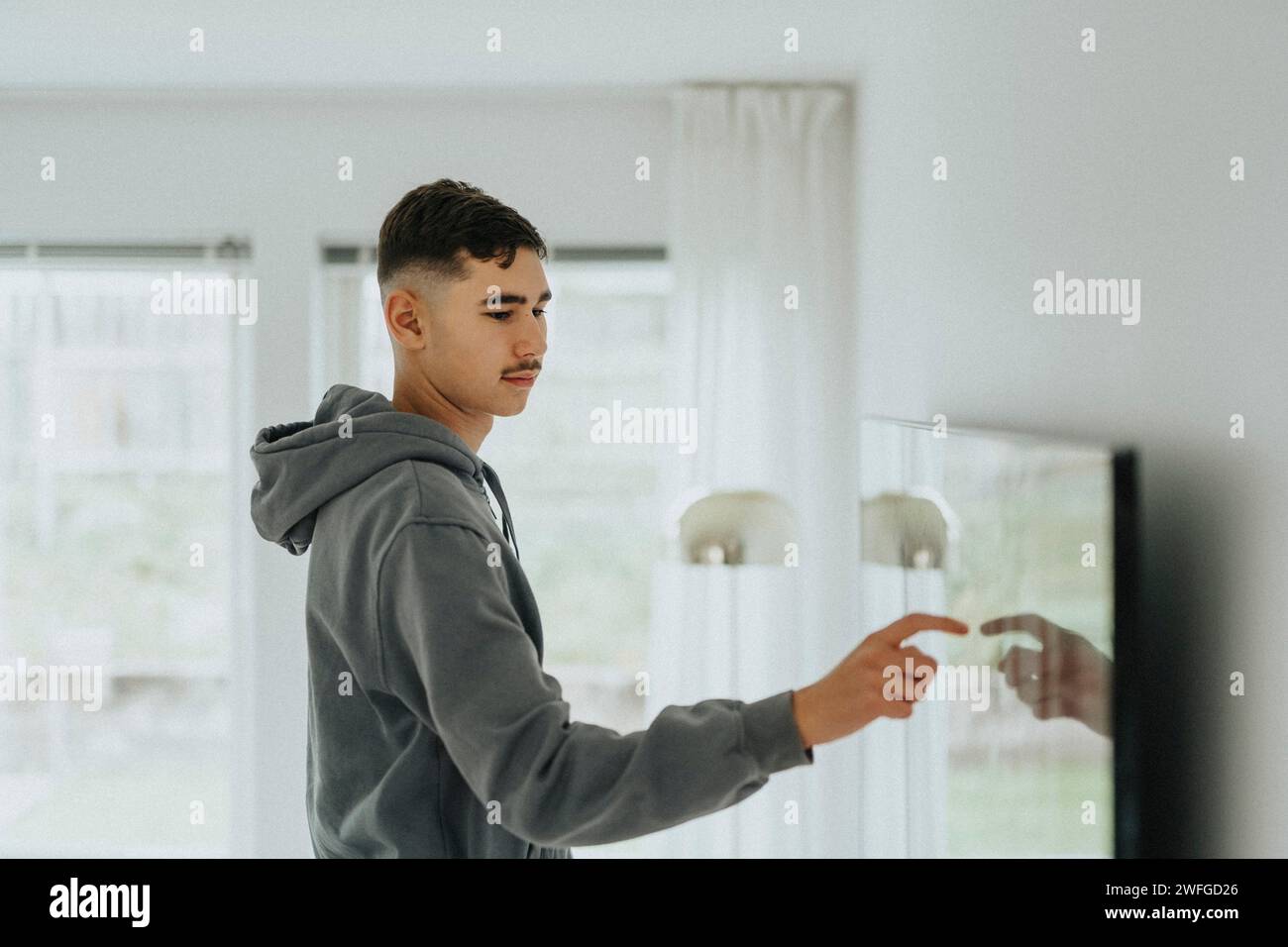 Side view of teenage boy touching smart TV screen in living room Stock ...
