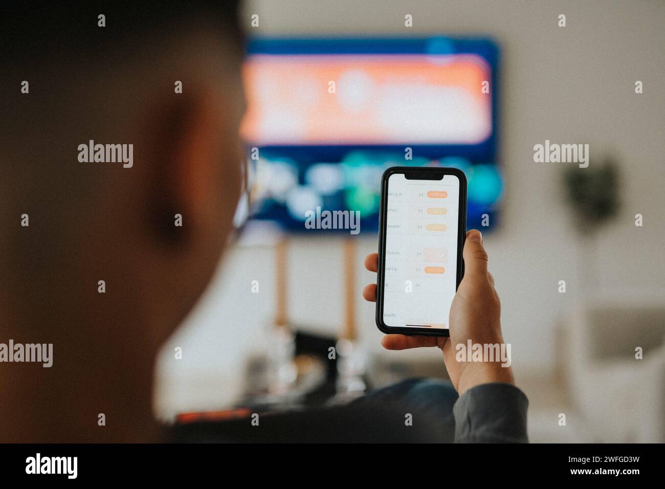 Teenage boy using smart phone app while watching TV in living room at ...