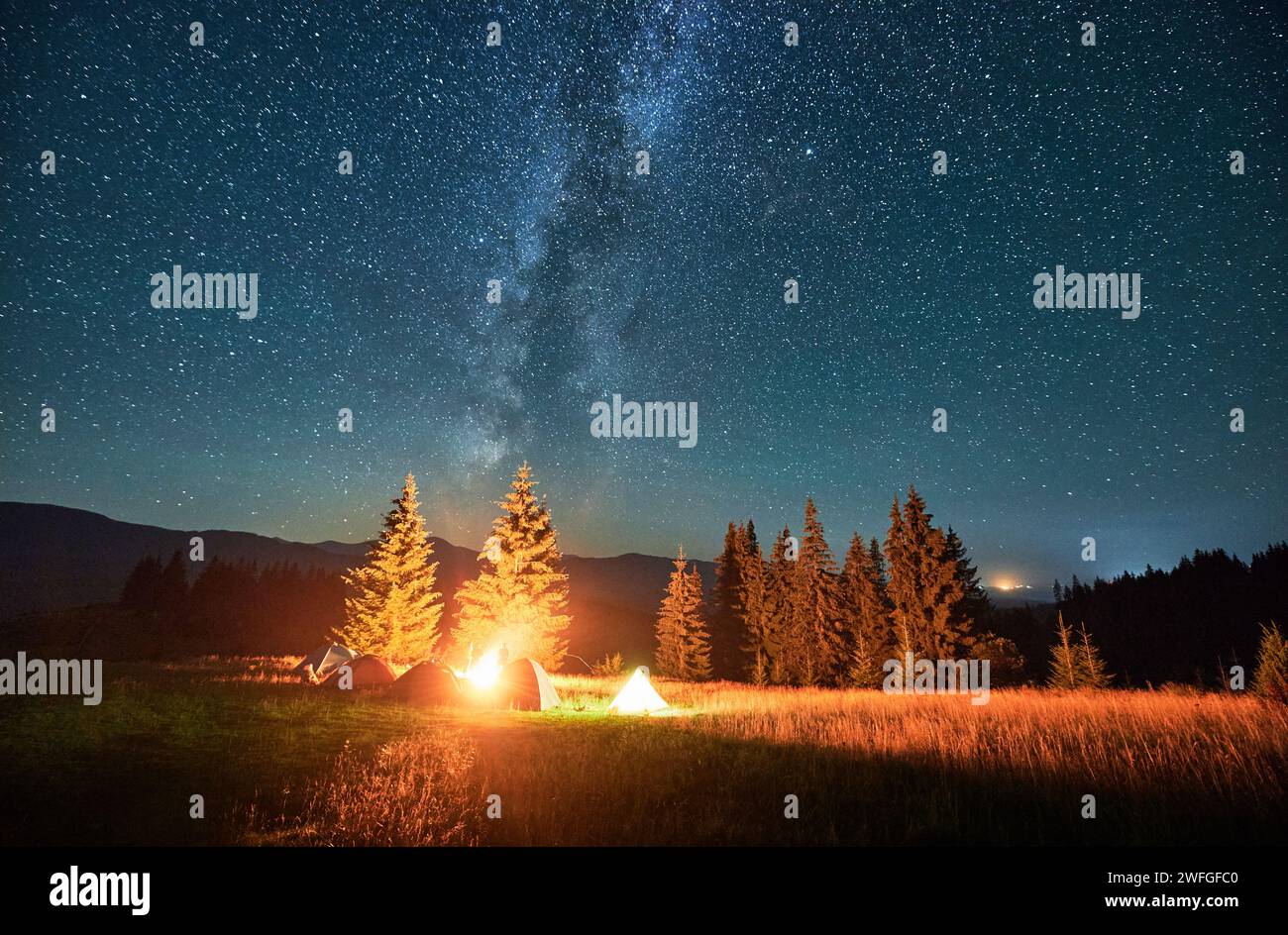 Night camping in mountains under starry sky and Milky way. Tents standing in campsite, fire ...