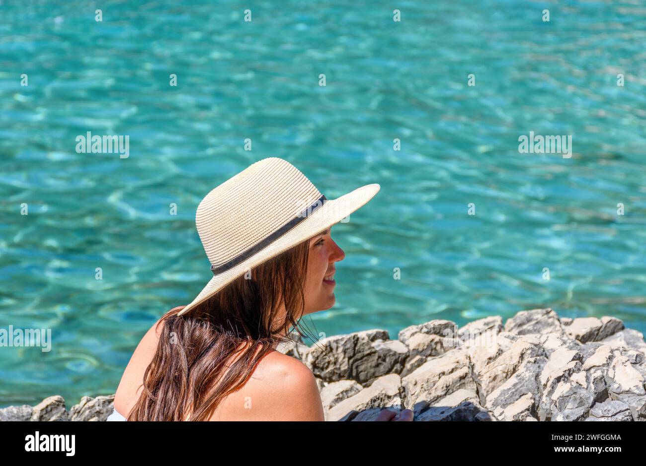 Side view of female tourist wearing sun hat while sunbathing on rocky ...