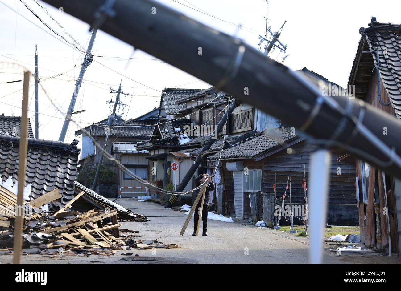 A man supports a cable of utility pole with wood so that cars can pass ...