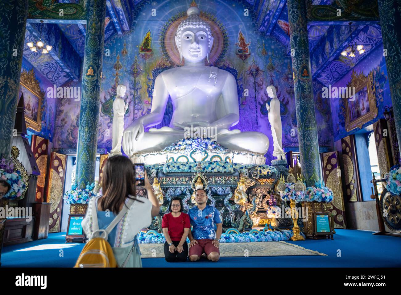 Locals take pictures in front of the white sitting Buddha statue inside ...