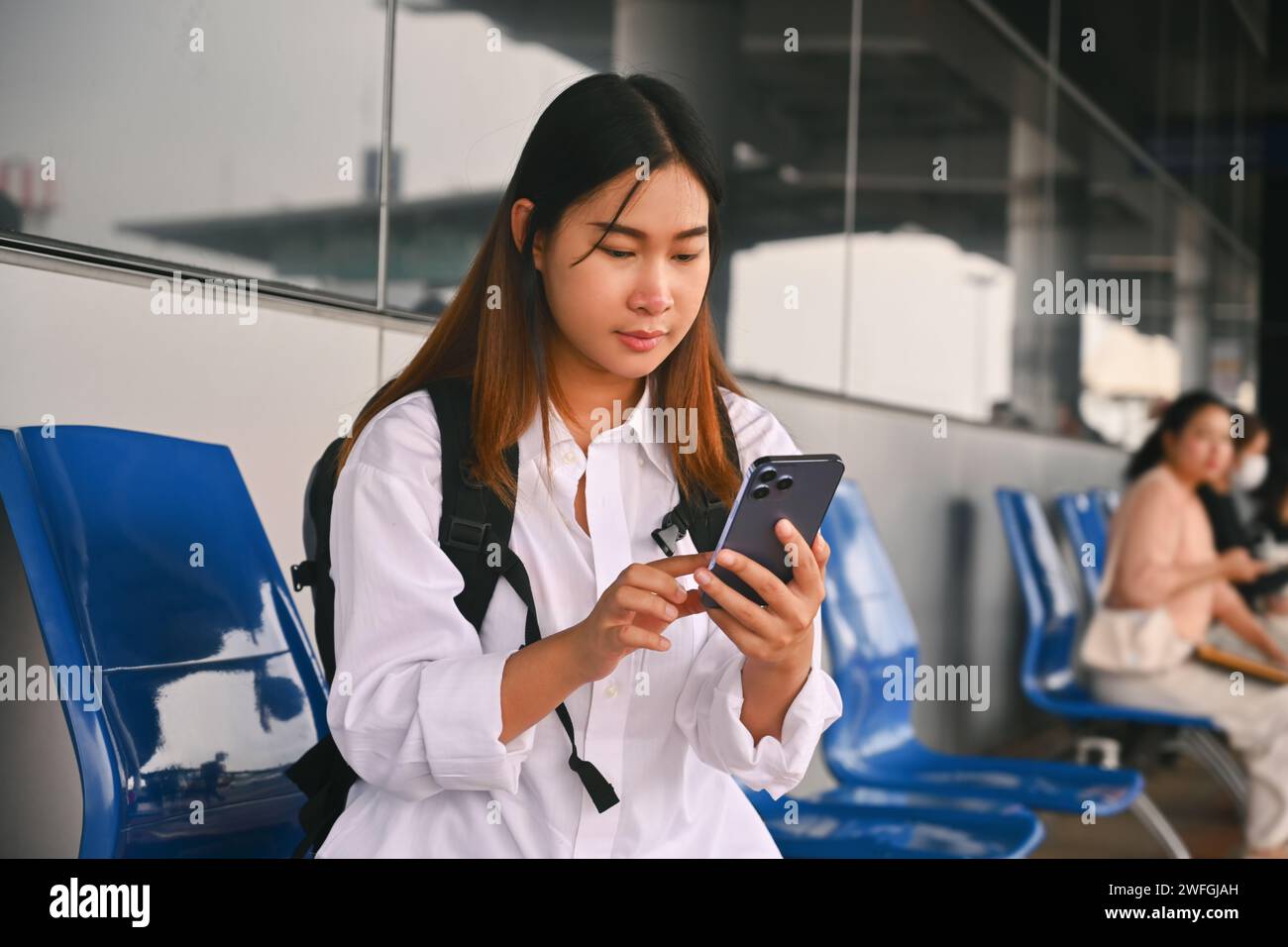 Young woman sitting at bus station, waiting for bus and using mobile ...
