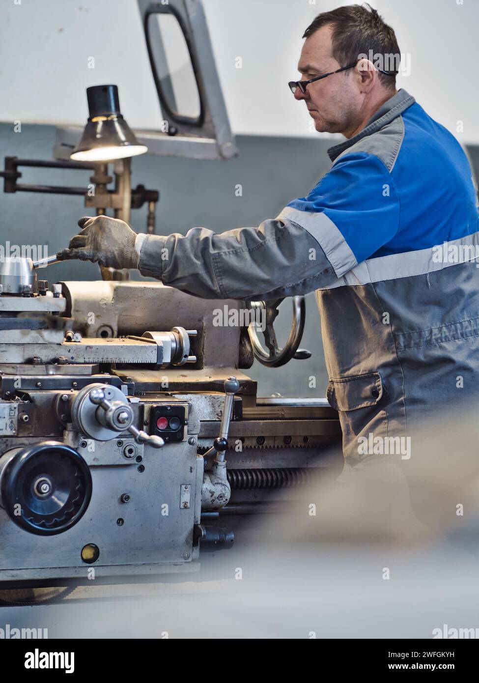 Turner in overalls works at lathe in turning shop at factory. Elderly ...