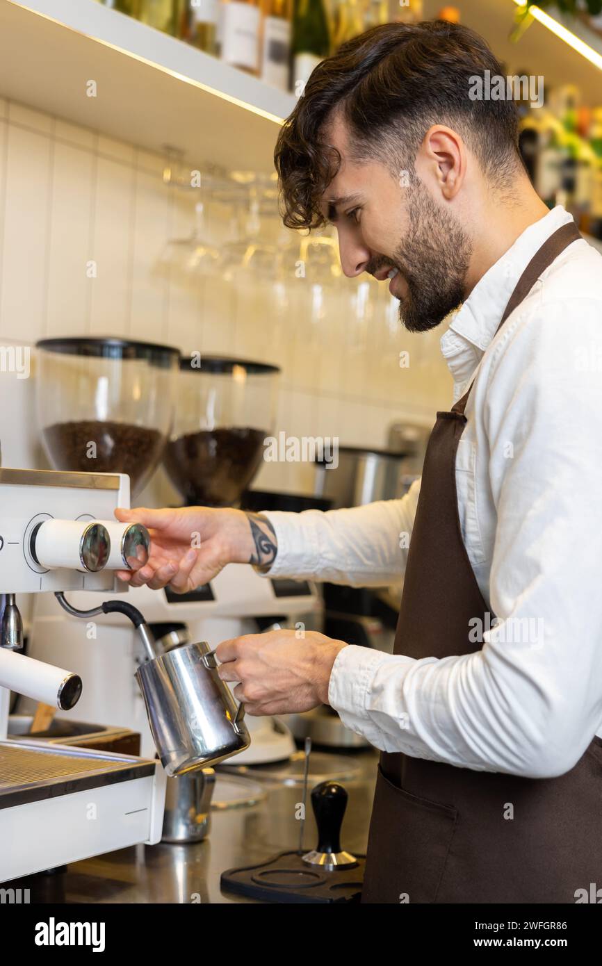 Smiling barista standing near coffee machine and looking contented ...