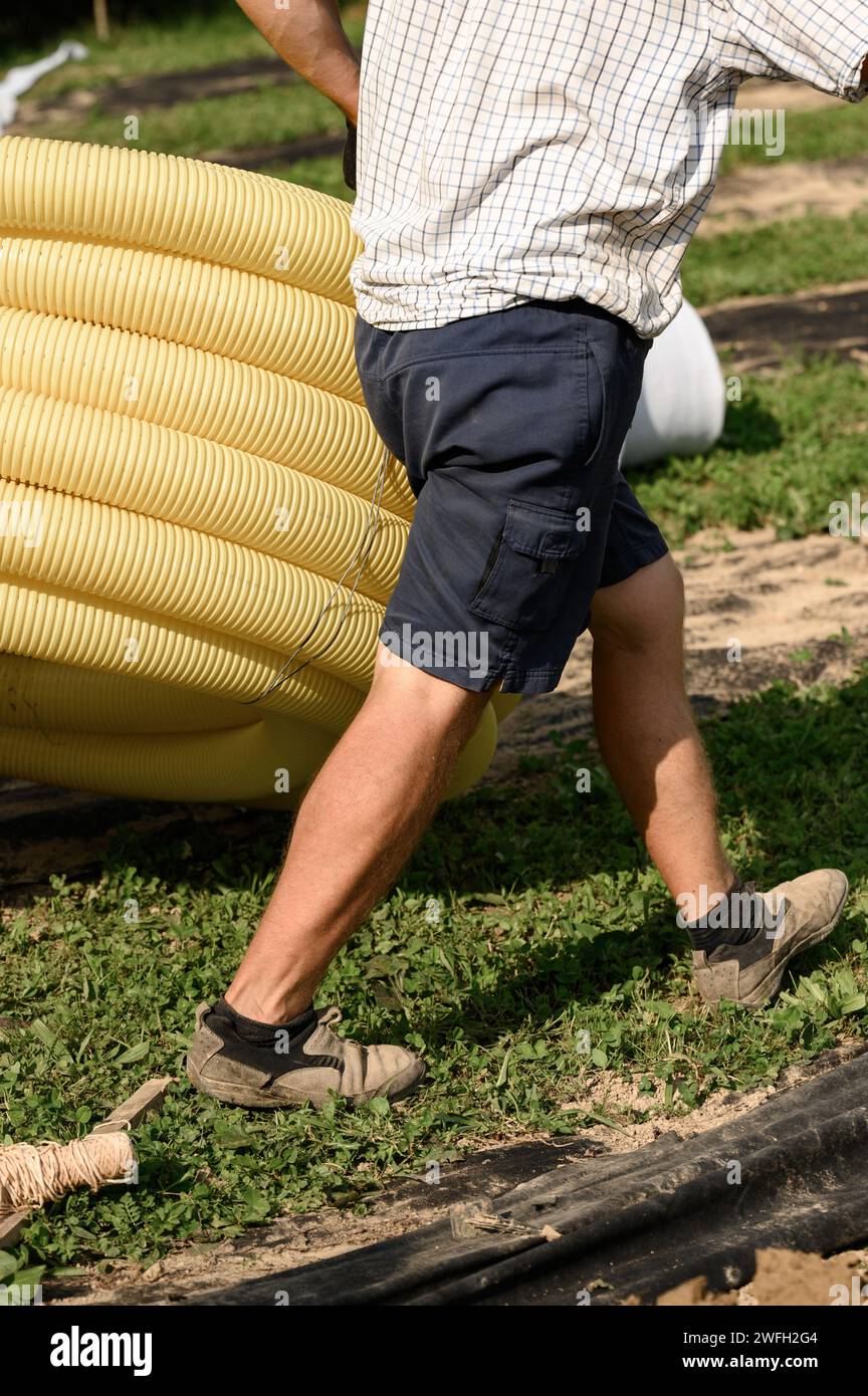 Workers carry a roll of yellow drainage pipe in their hands ...