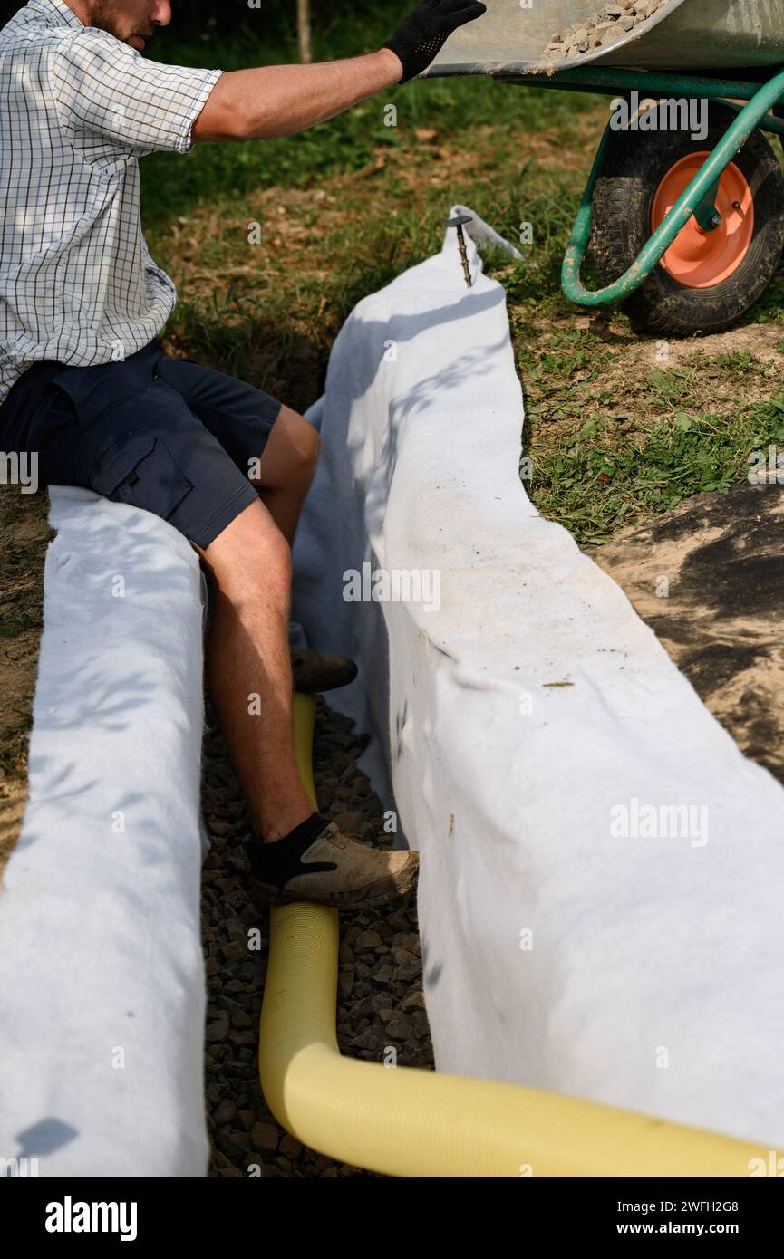 A worker stands in a drainage trench with white geotextile. Feet of the ...