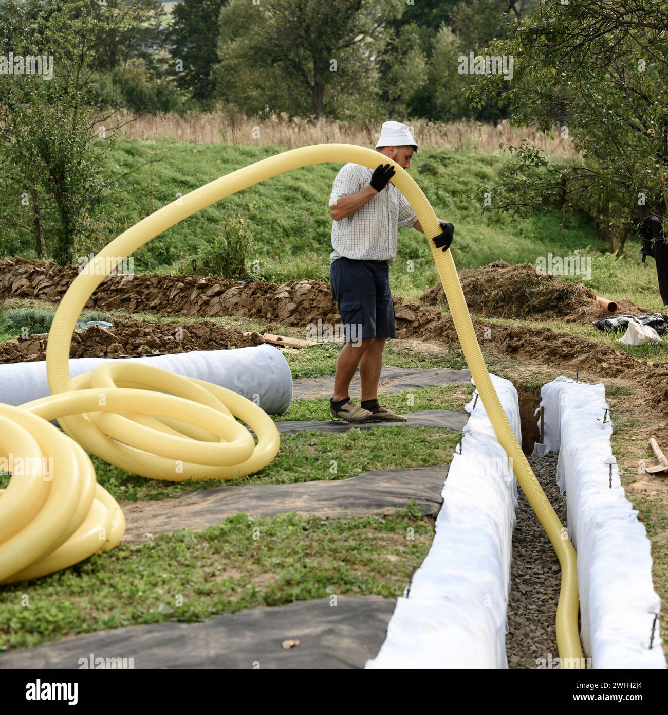 Groundwater drainage works in the field. A worker carries a yellow ...