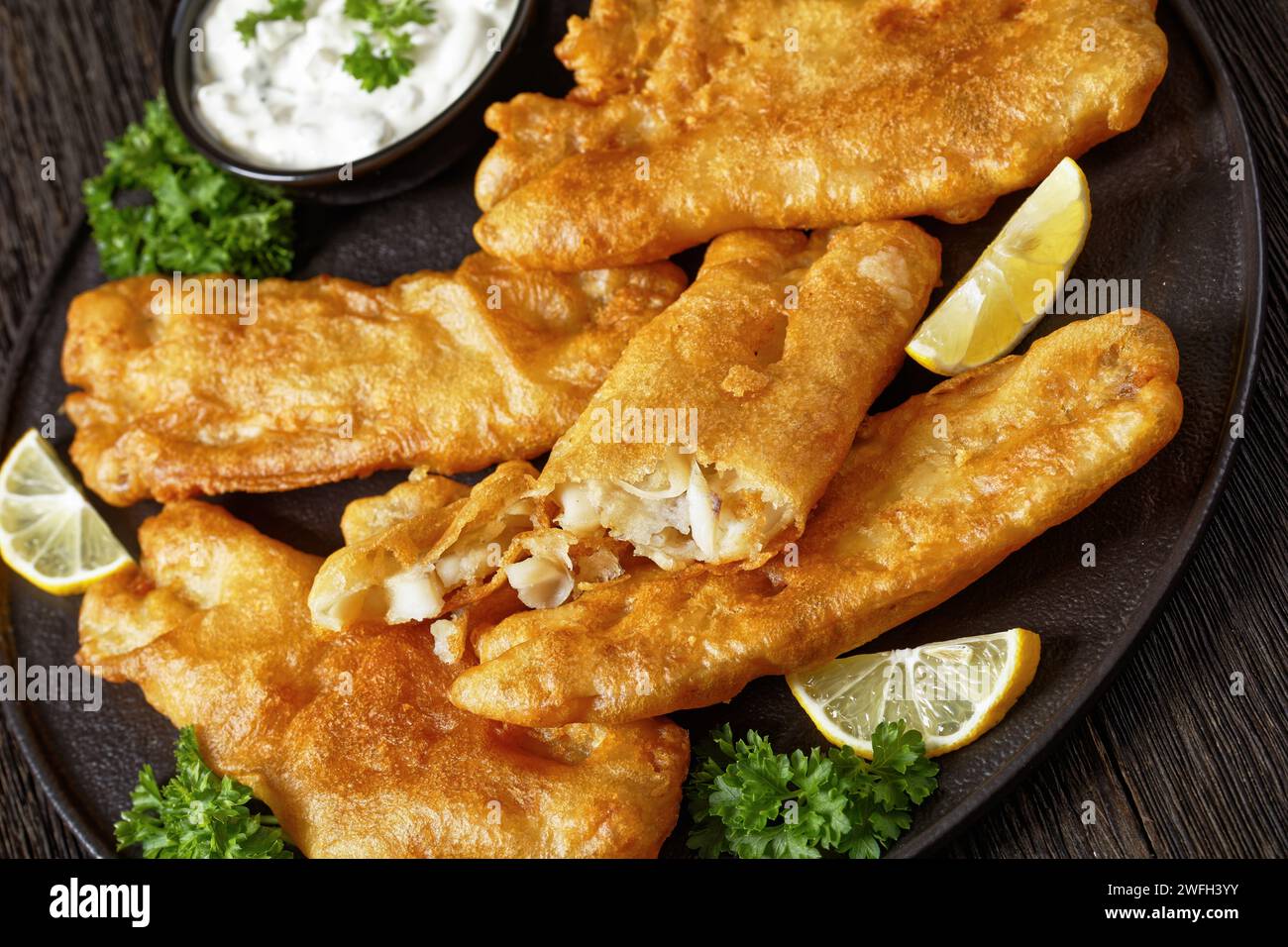 deep fried crispy beer batter fish fillet on black plate with tartar ...