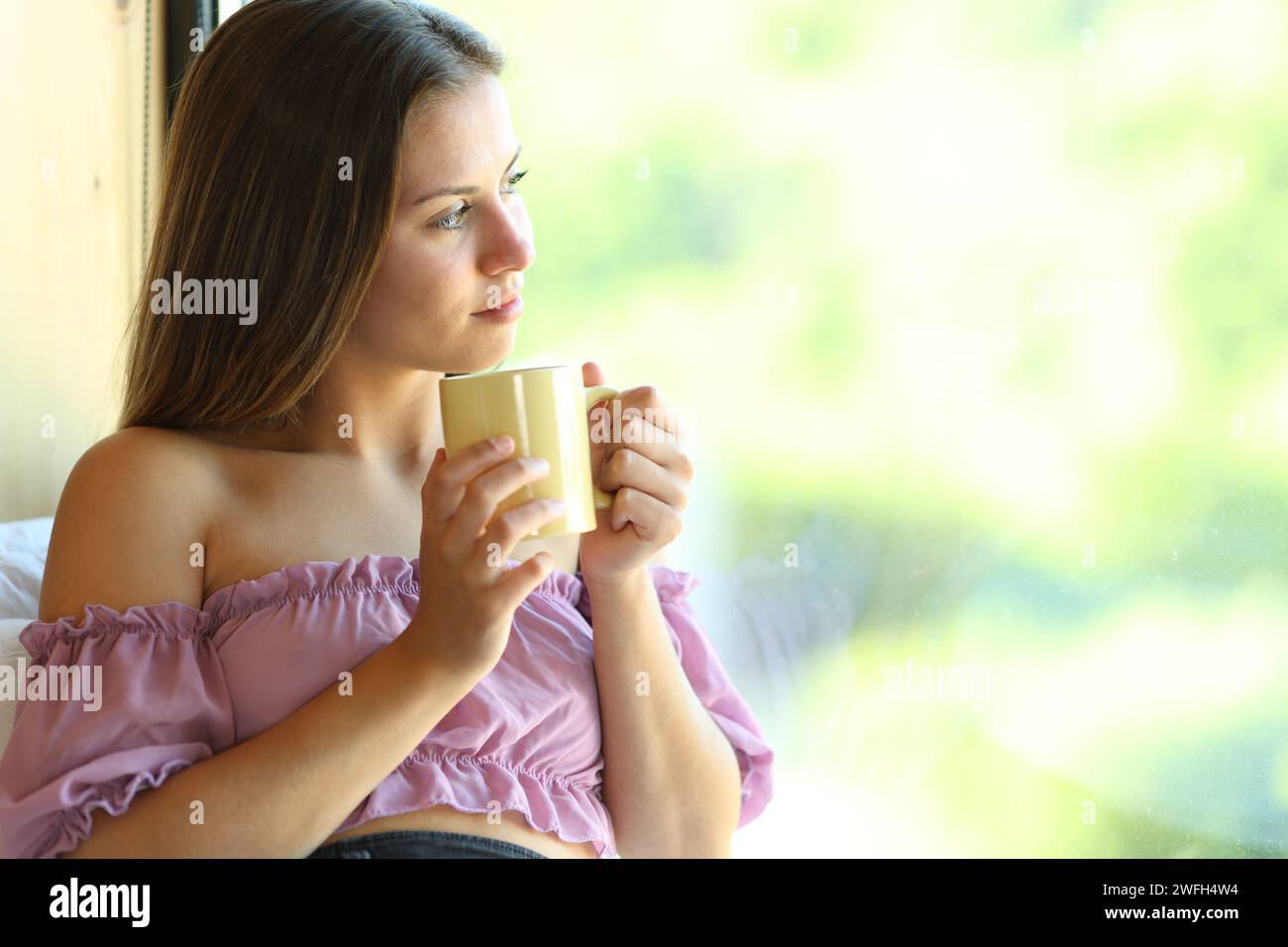Teen looking through a window drinking tea at home Stock Photo - Alamy