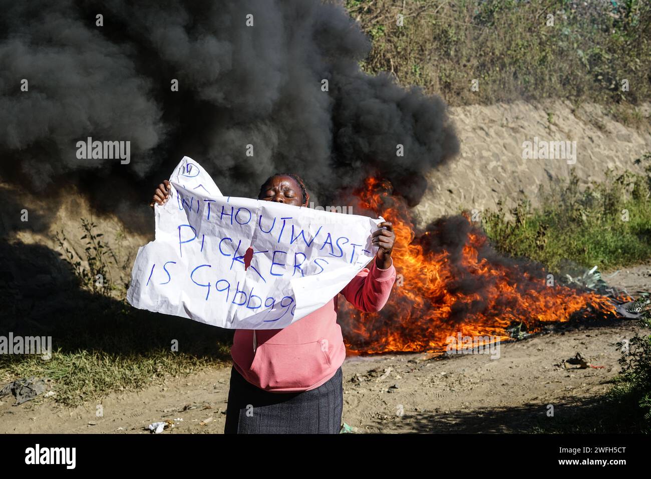A waste picker holds a placard in front of a smoky bonfire during a ...