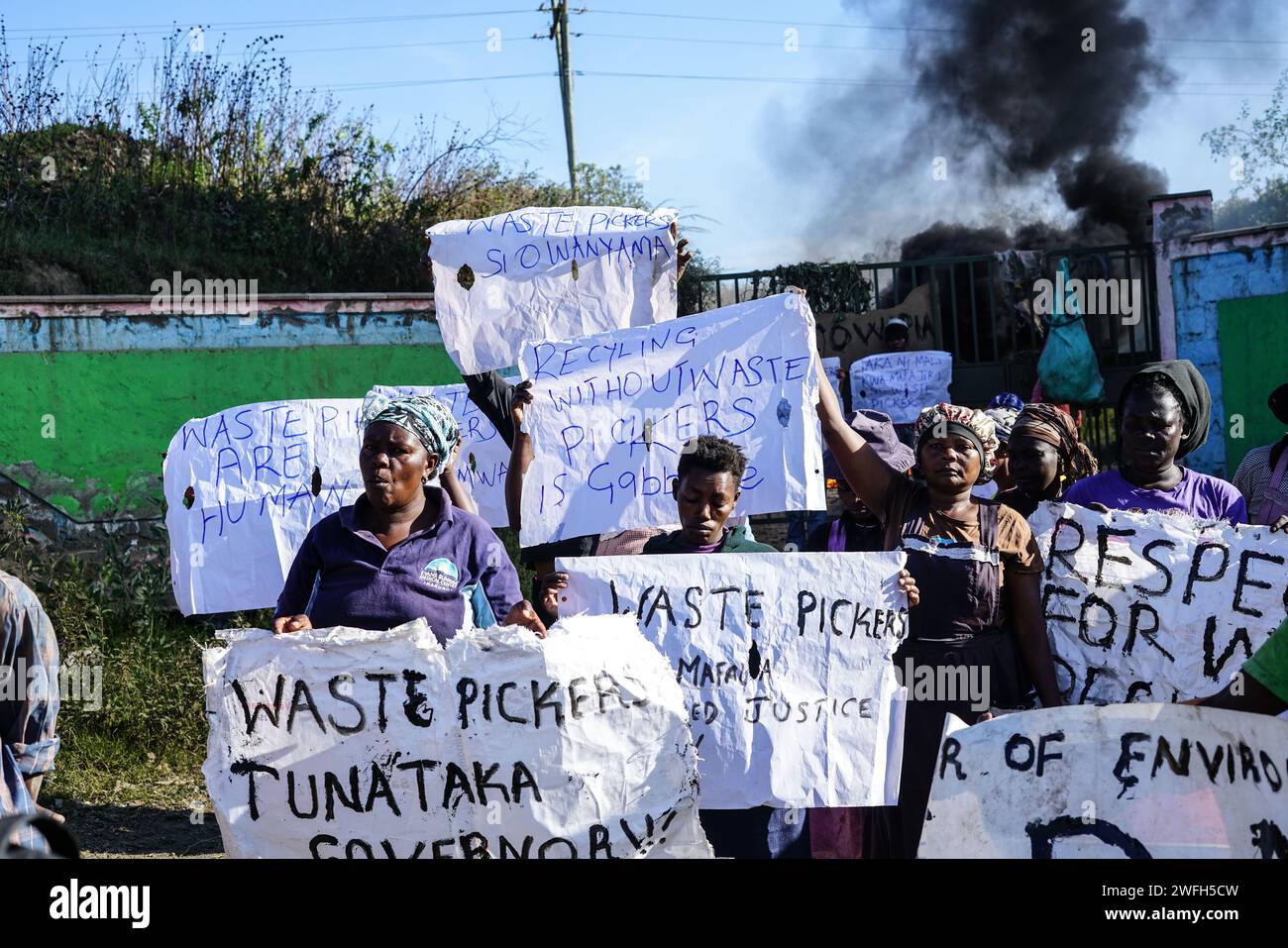 Waste pickers hold placards in front of a smoky bonfire during a ...