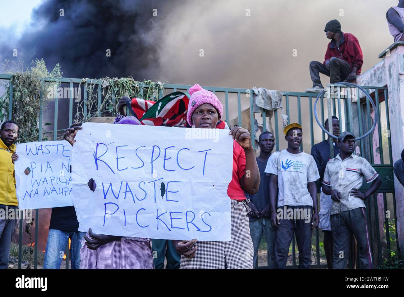 Waste pickers hold placards in front of a smoky bonfire during a ...