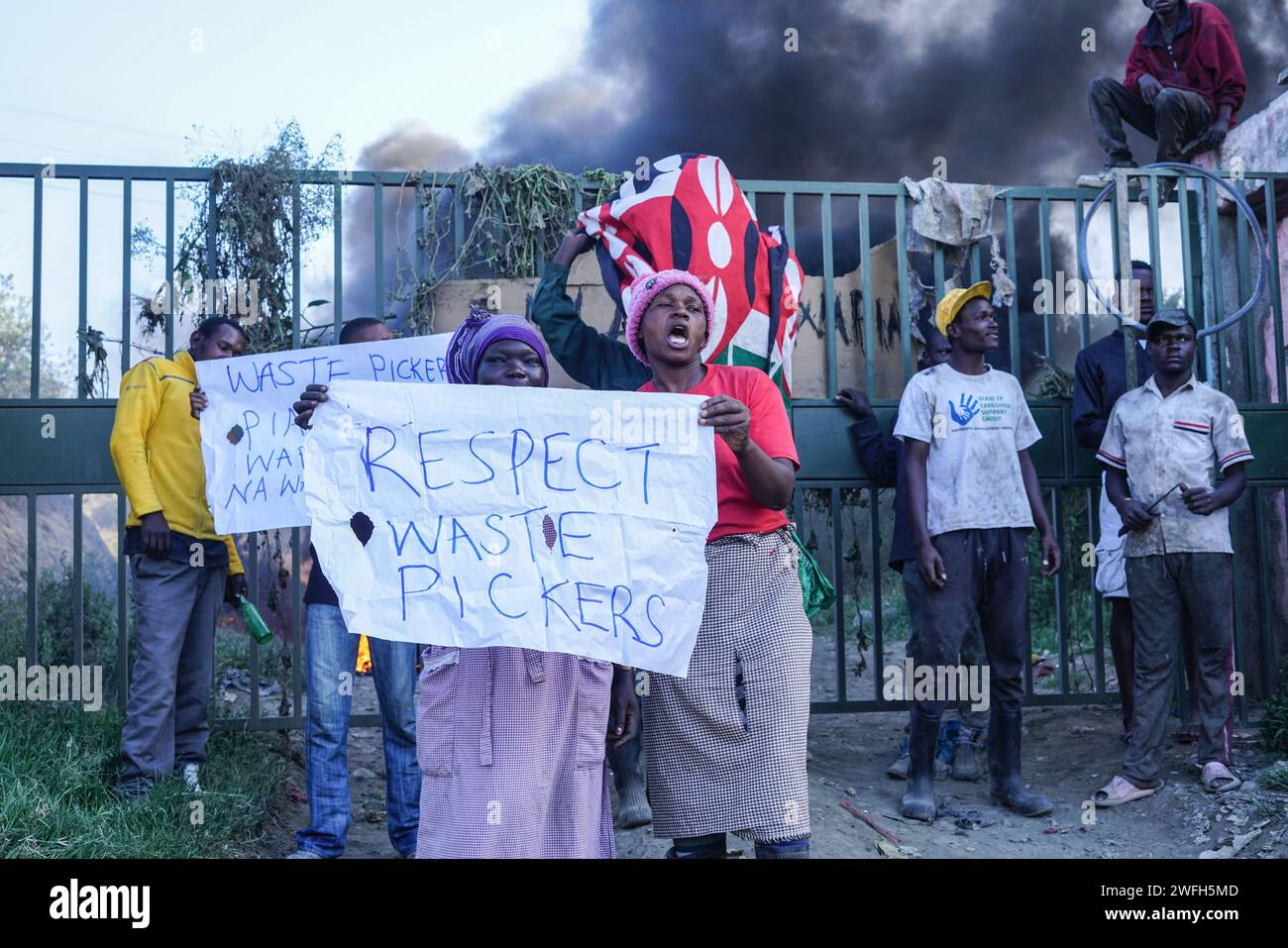 Waste pickers chant slogans hold placards in front of a smoky bonfire ...