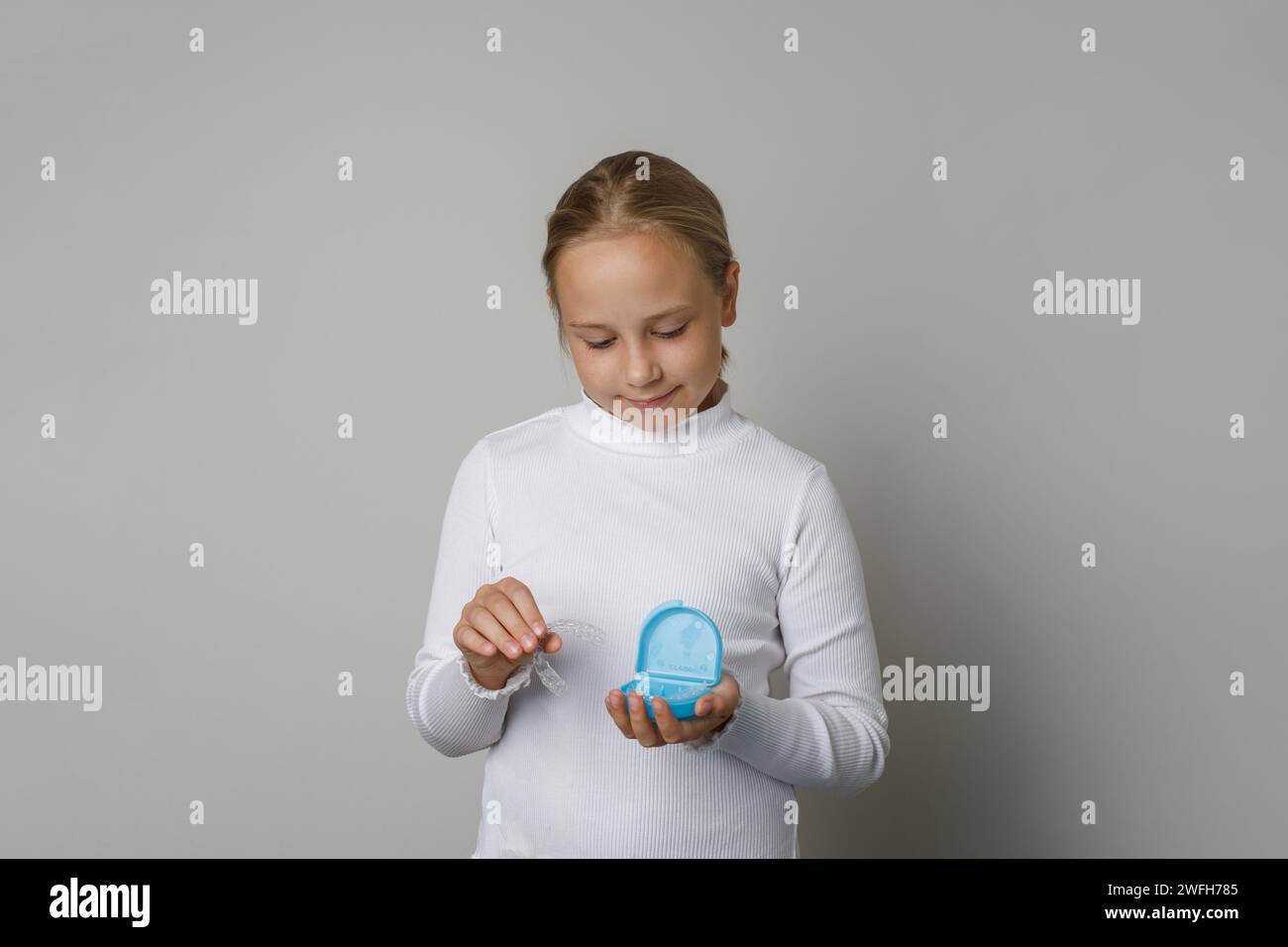 Cute child girl wearing white t-shirt holding an invisible aligner ...