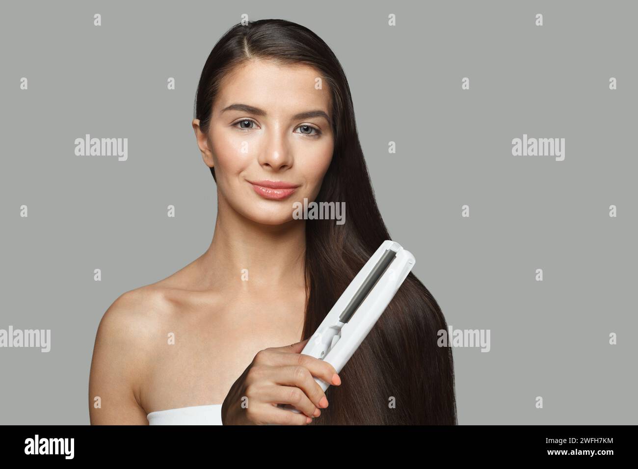 Brunette model woman holding hair iron and straightening her healthy ...