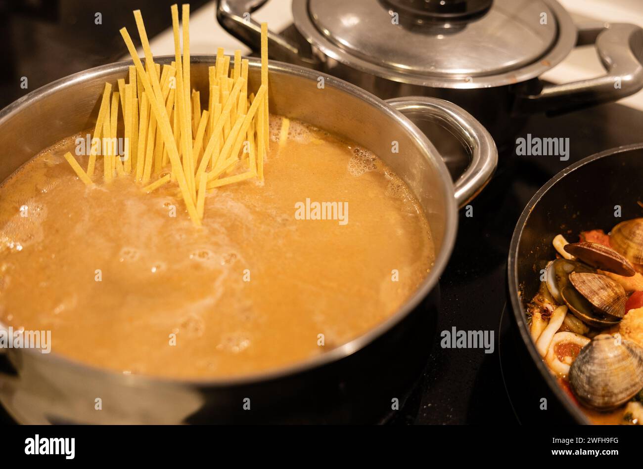Golden pasta stands tall in boiling water next to a pot of simmering ...