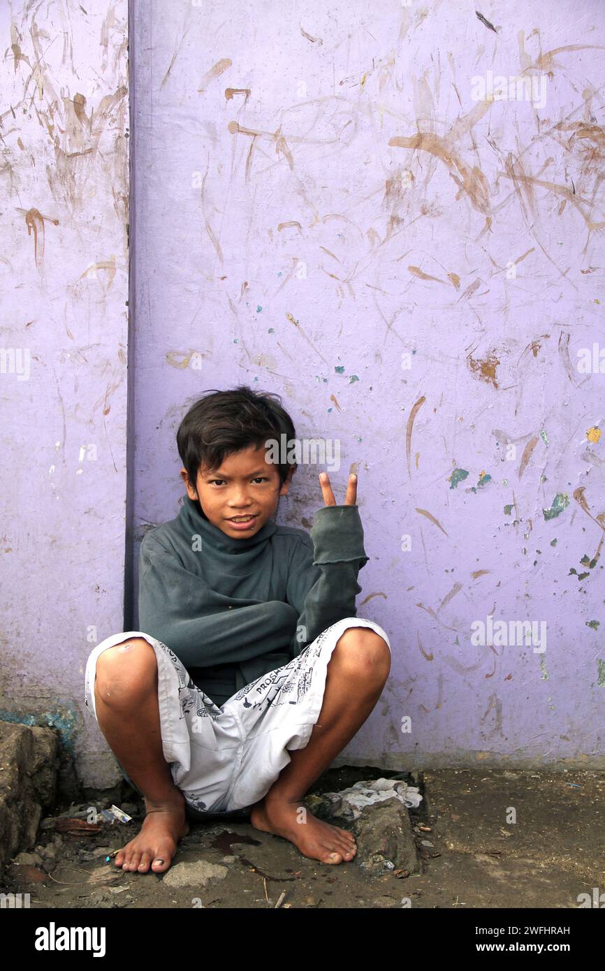 A street kid sitting against a purple colored wall in Bandung, West ...