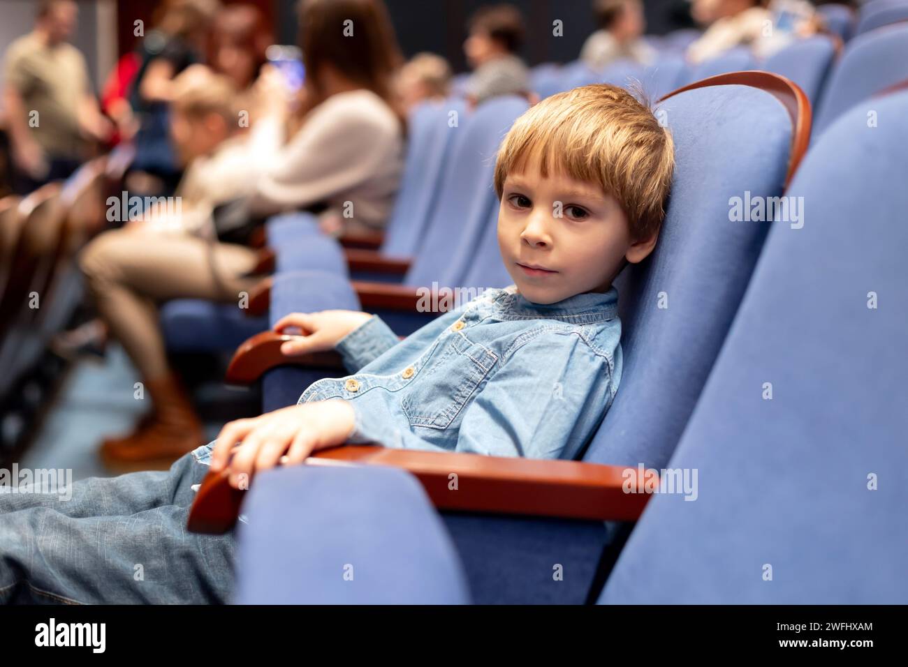 Cute child, boy, sitting in a theater, wating for the show to start ...