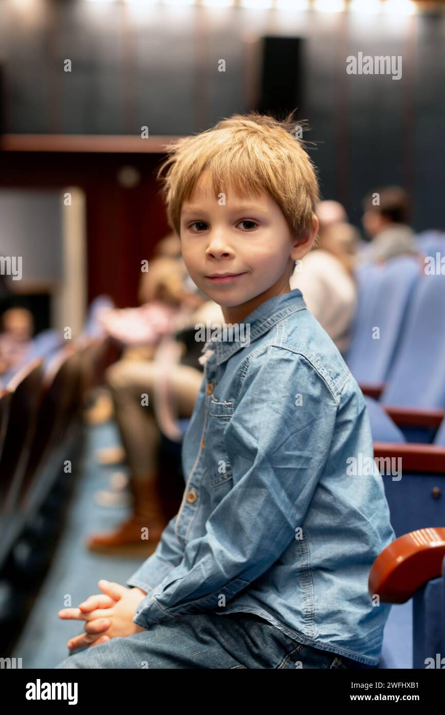 Cute child, boy, sitting in a theater, wating for the show to start ...