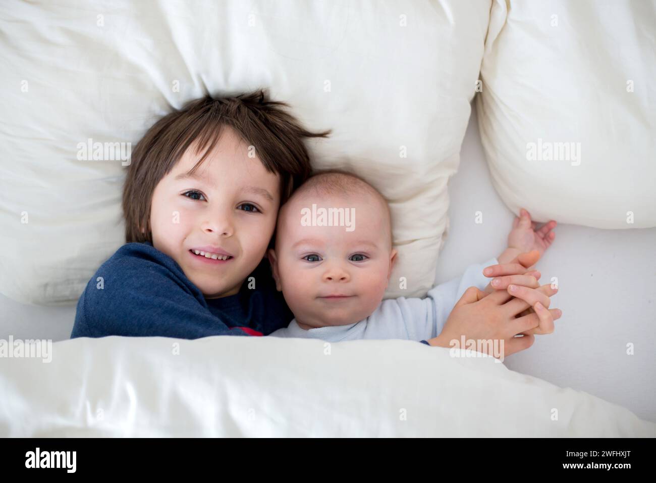 Two children, baby and his older brother in bed in the morning, playing ...