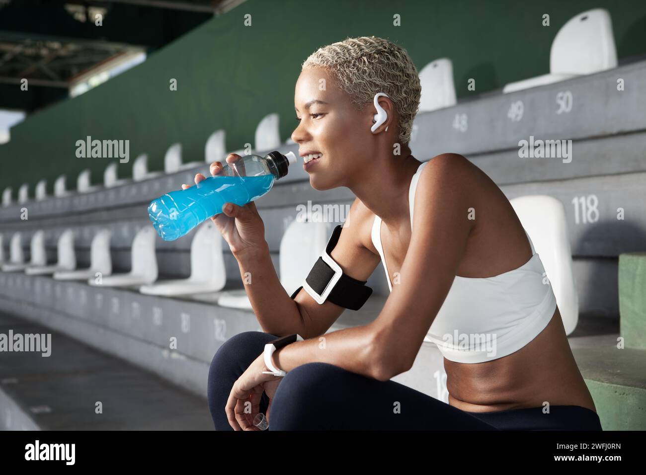 Smiling female athlete drinking energy drink from bottle after running ...