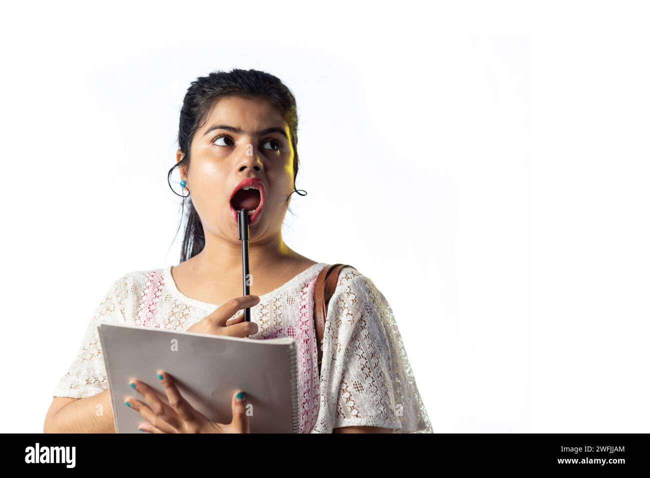 A pretty young Indian girl thinking while taking notes and looking ...
