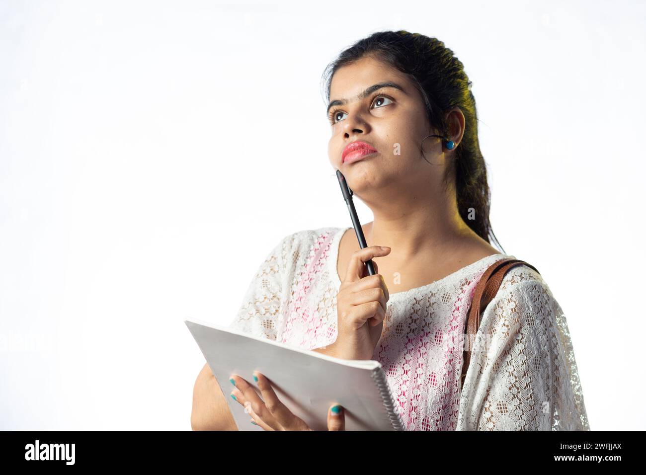 A pretty young Indian girl thinking and taking notes on white ...