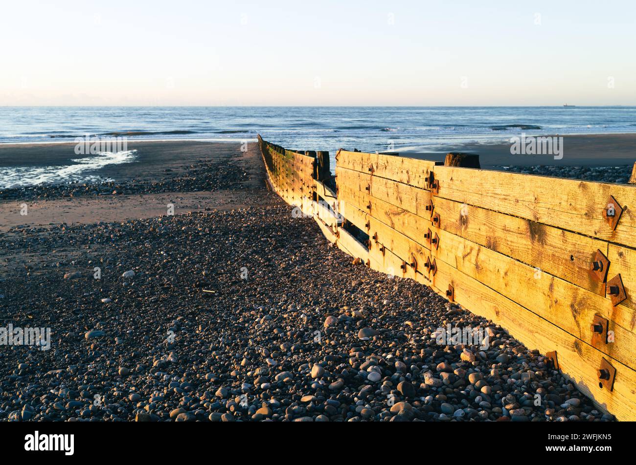 sand and pebble beach in the UK early evening sunlight with wooden ...