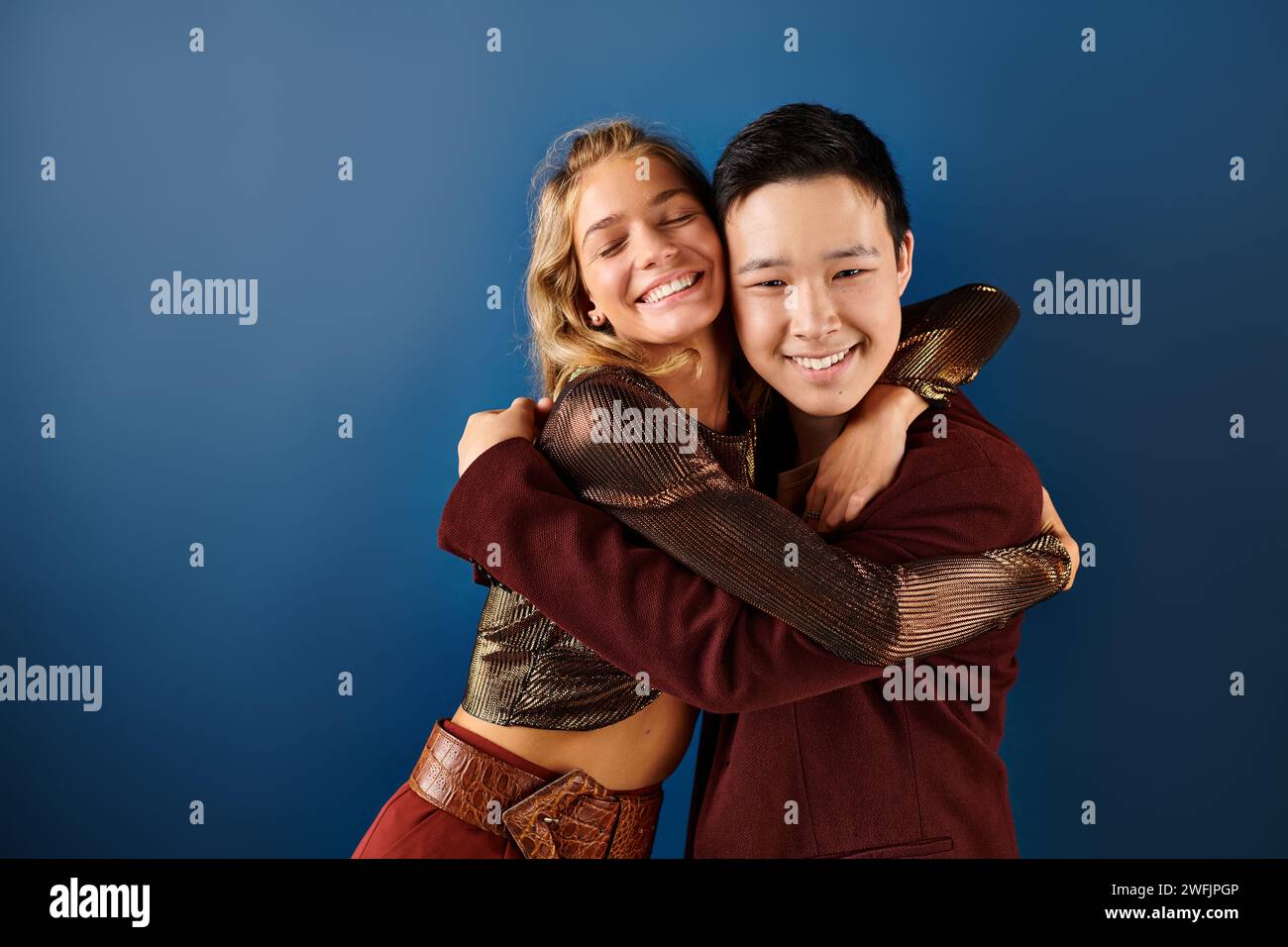 cheerful adolescent blonde girl and asian boy hugging and smiling at ...