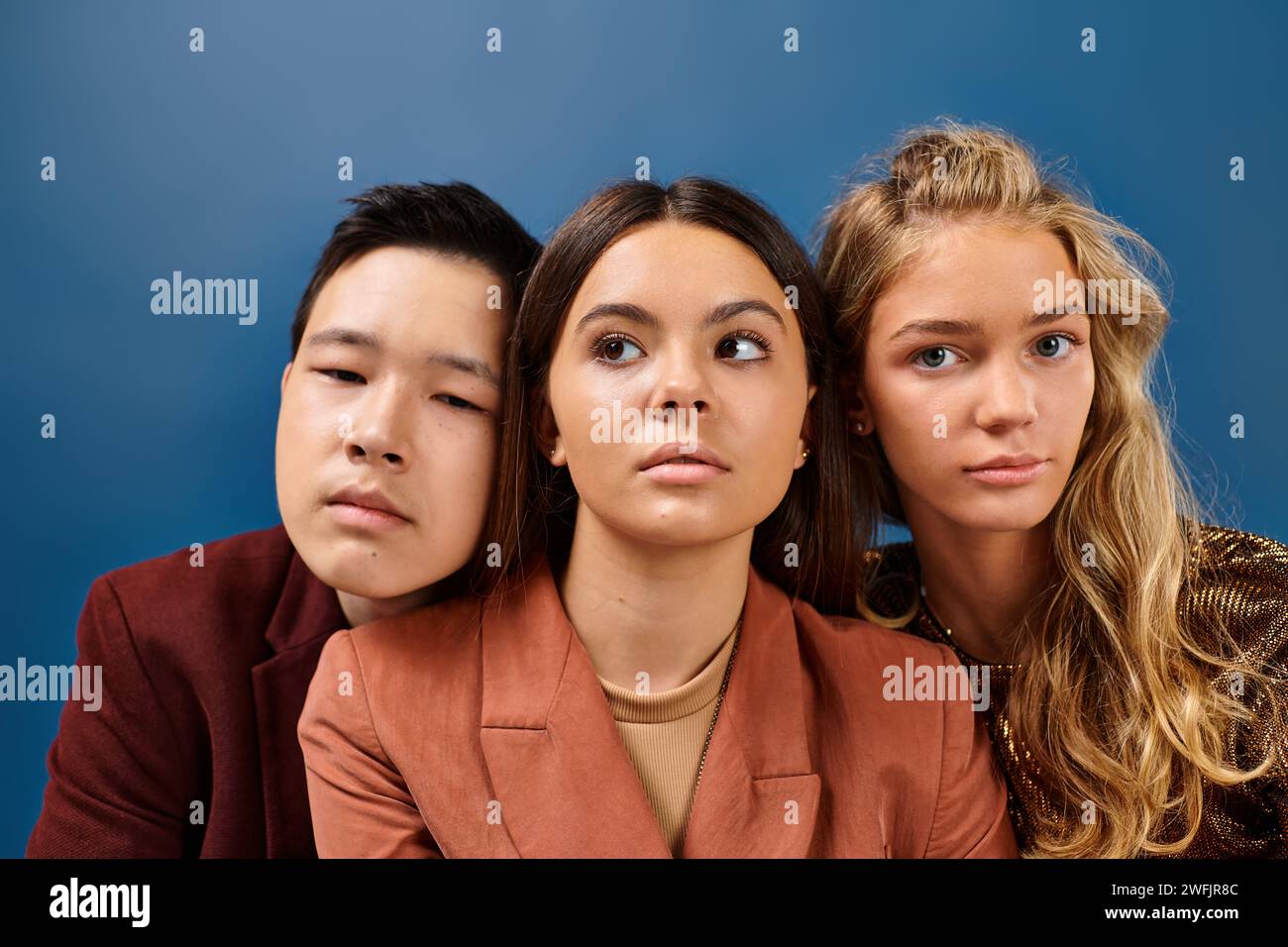 multicultural fashionable teens in elegant outfits posing on blue ...