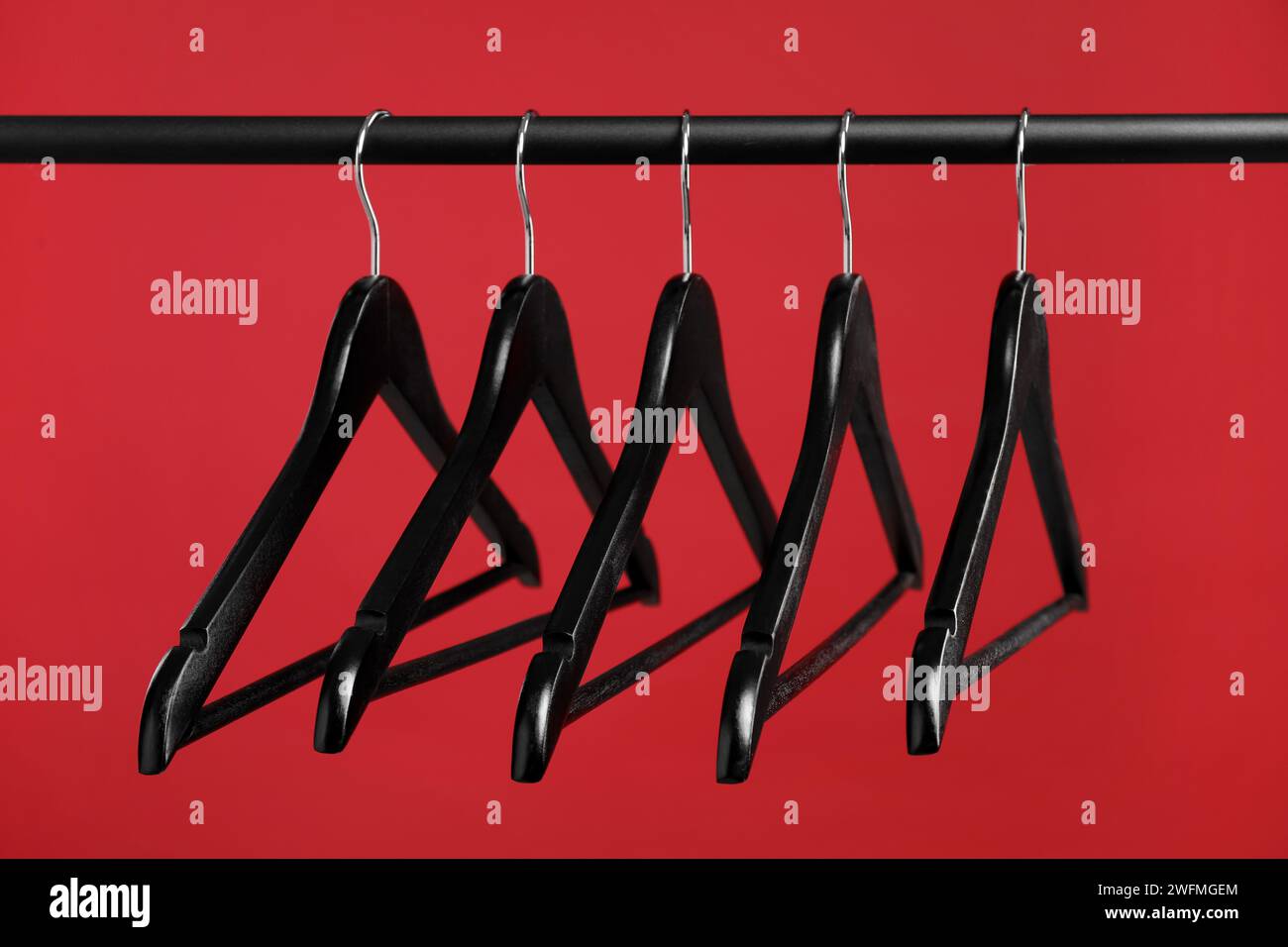 Black clothes hangers on rack against red background Stock Photo - Alamy