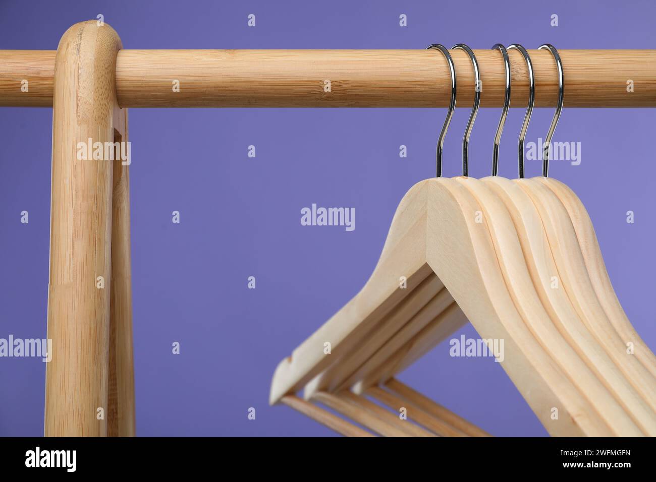 Empty clothes hangers on wooden rack against purple background, closeup ...