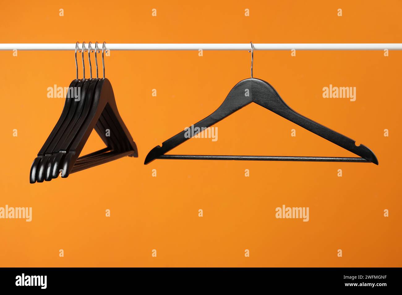 Black clothes hangers on rack against orange background Stock Photo - Alamy