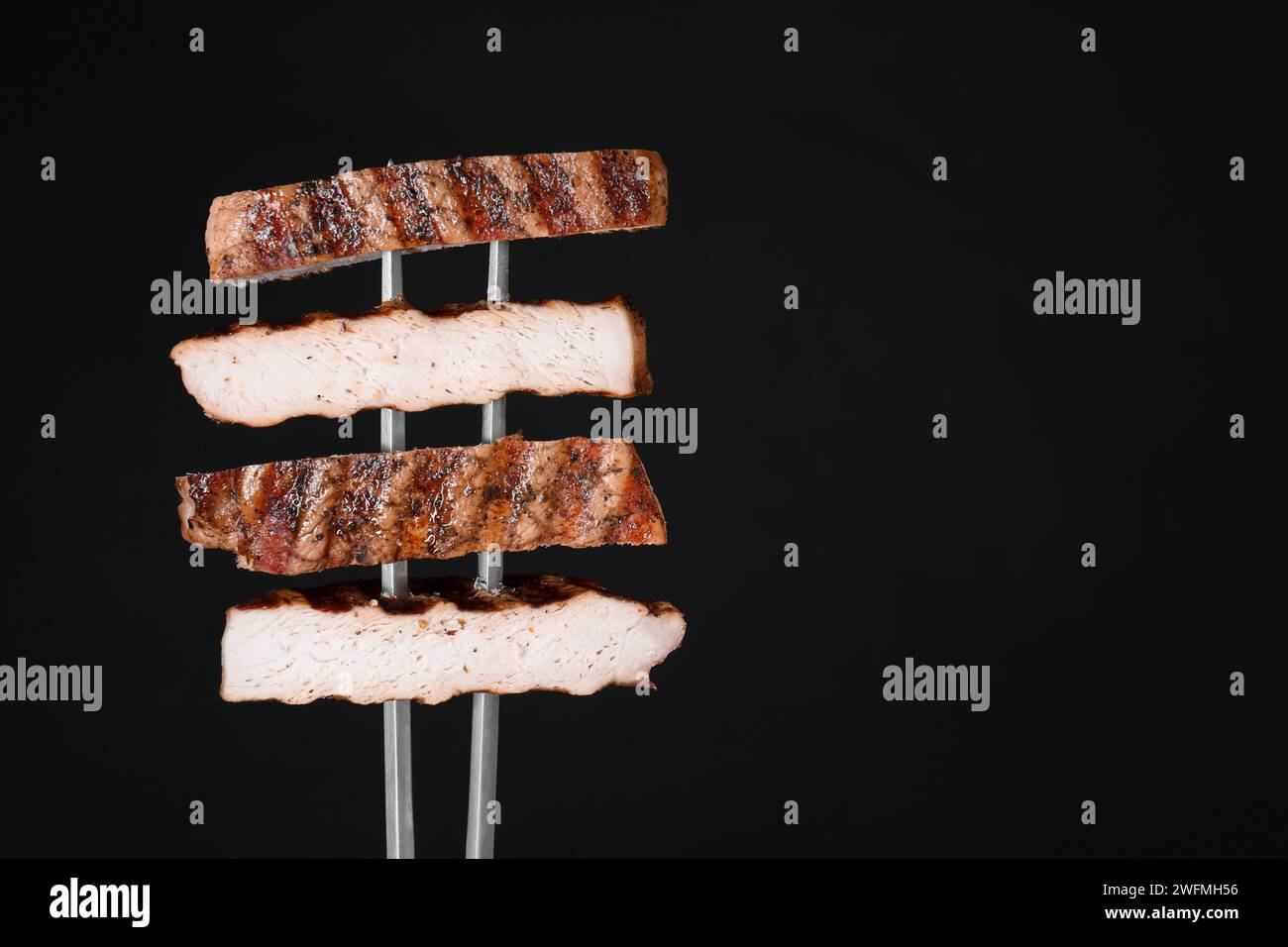 Carving fork with cut grilled pork steak pieces against black ...