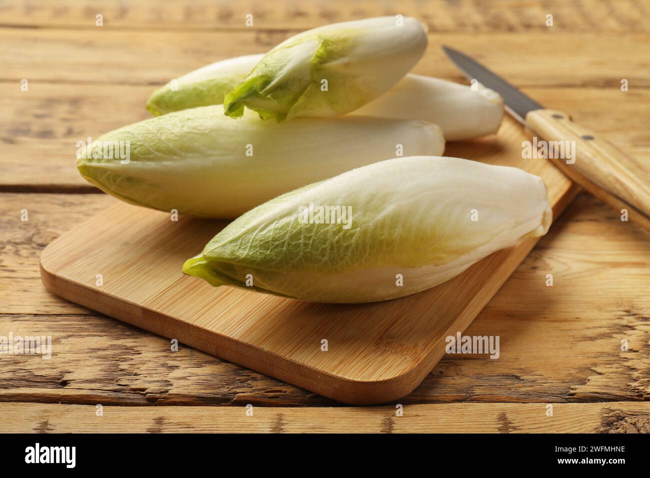 Fresh raw Belgian endives (chicory), board and knife on wooden table, closeup Stock Photo - Alamy