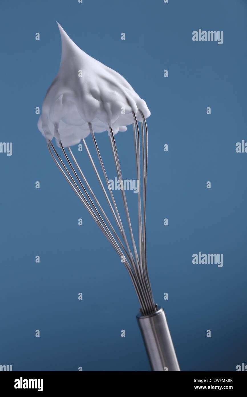 Whisk with whipped cream on light blue background Stock Photo - Alamy