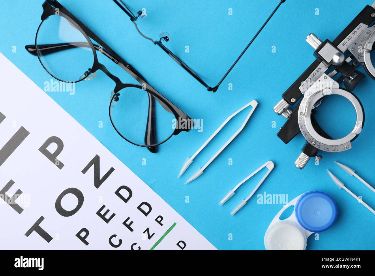 Flat lay composition with vision test chart and glasses on light blue ...